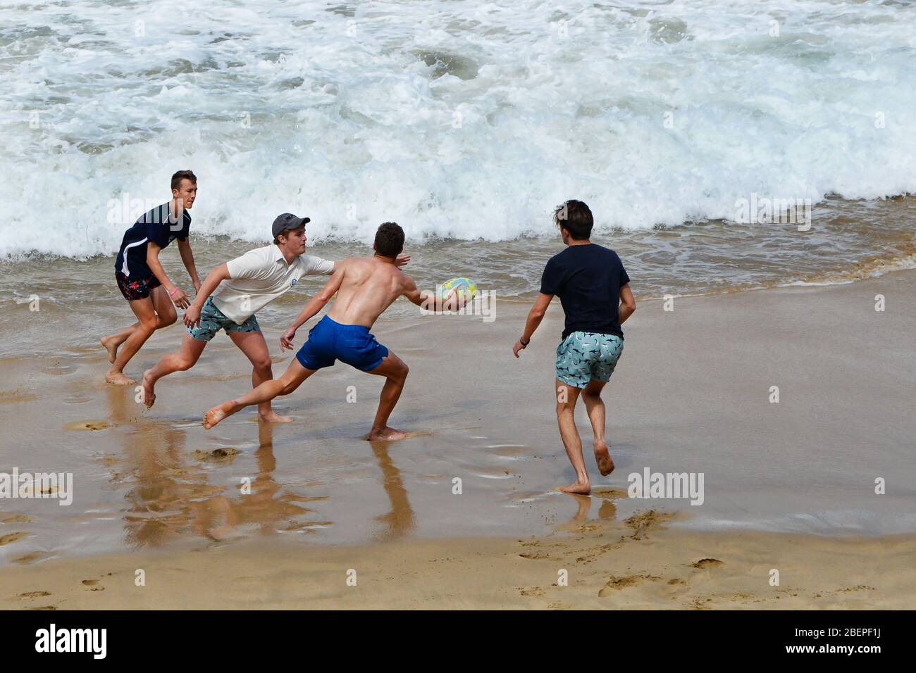 Four fit white South African teenagers play rugby on the beach in ...