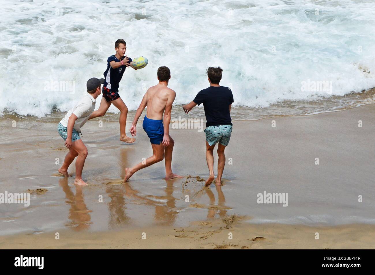 Four fit white South African teenagers play rugby on the beach in ...