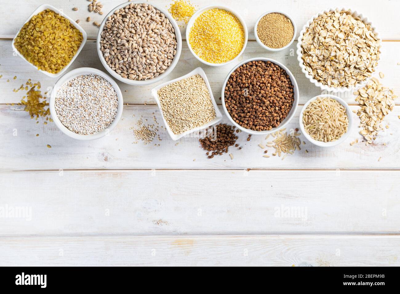 Selection of whole grains in white bowls - rice, oats, buckwheat ...