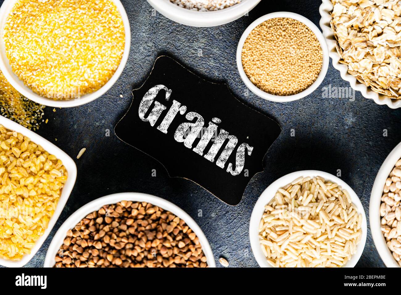 Selection of whole grains in white bowls - rice, oats, buckwheat ...