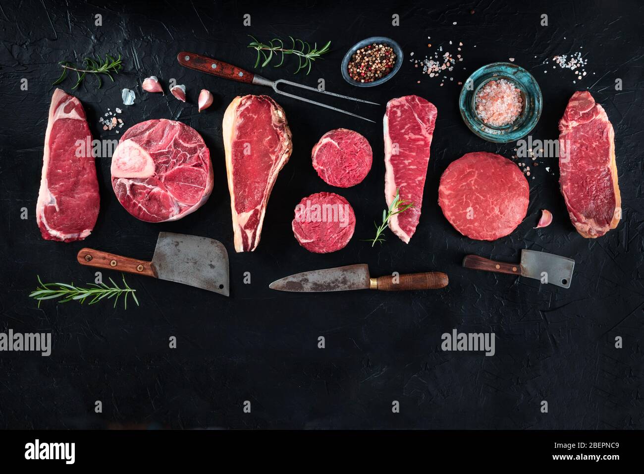 Various cuts of meat, shot from above on a black background with salt ...