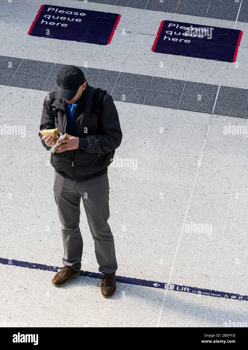 Man eating a sandwich whilst standing on a station concourse in London ...