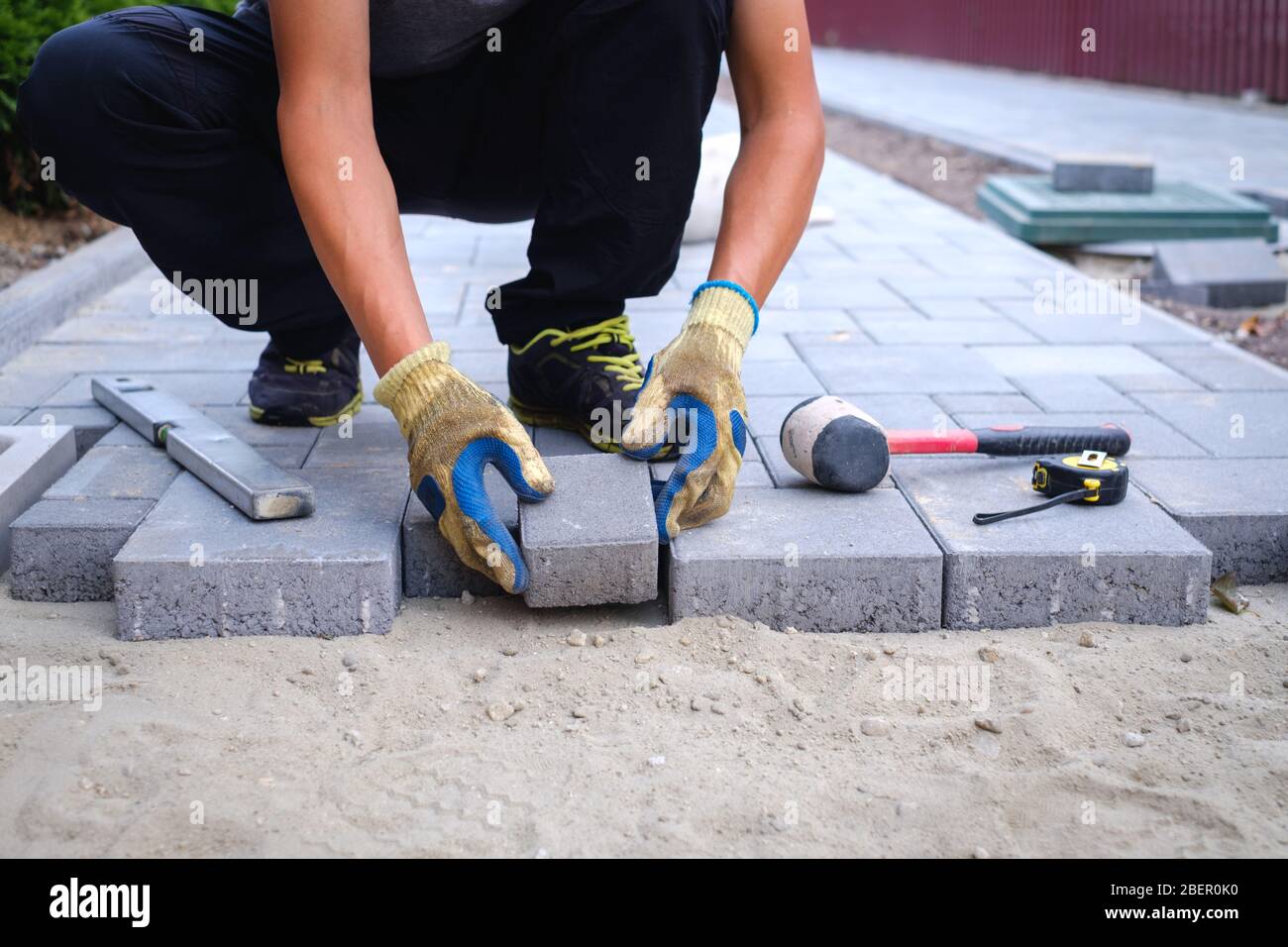 The master in yellow gloves lays paving stones in layers. Garden brick ...