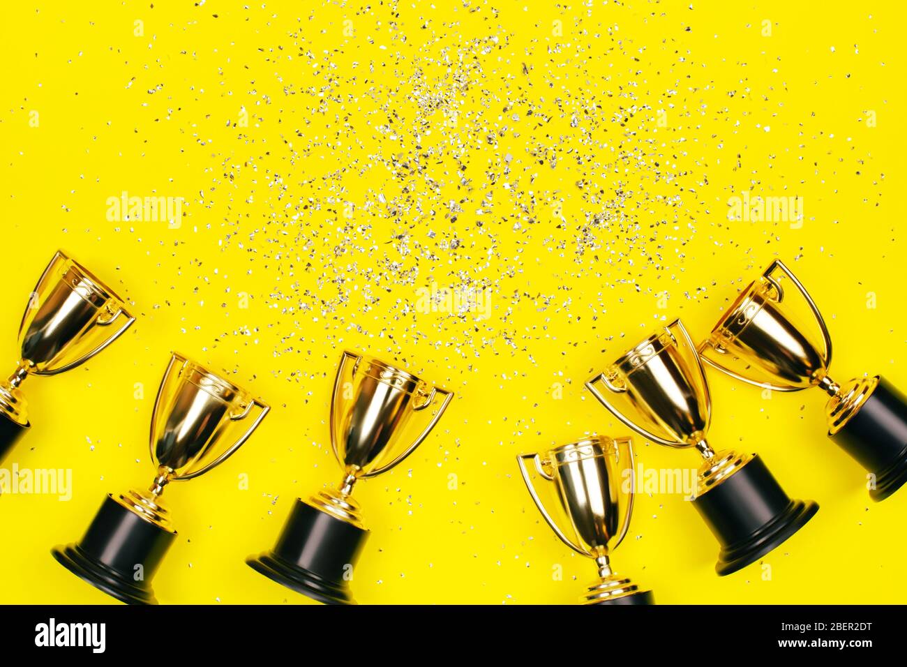 Golden winner cups with silver sparkles on a yellow background with ...
