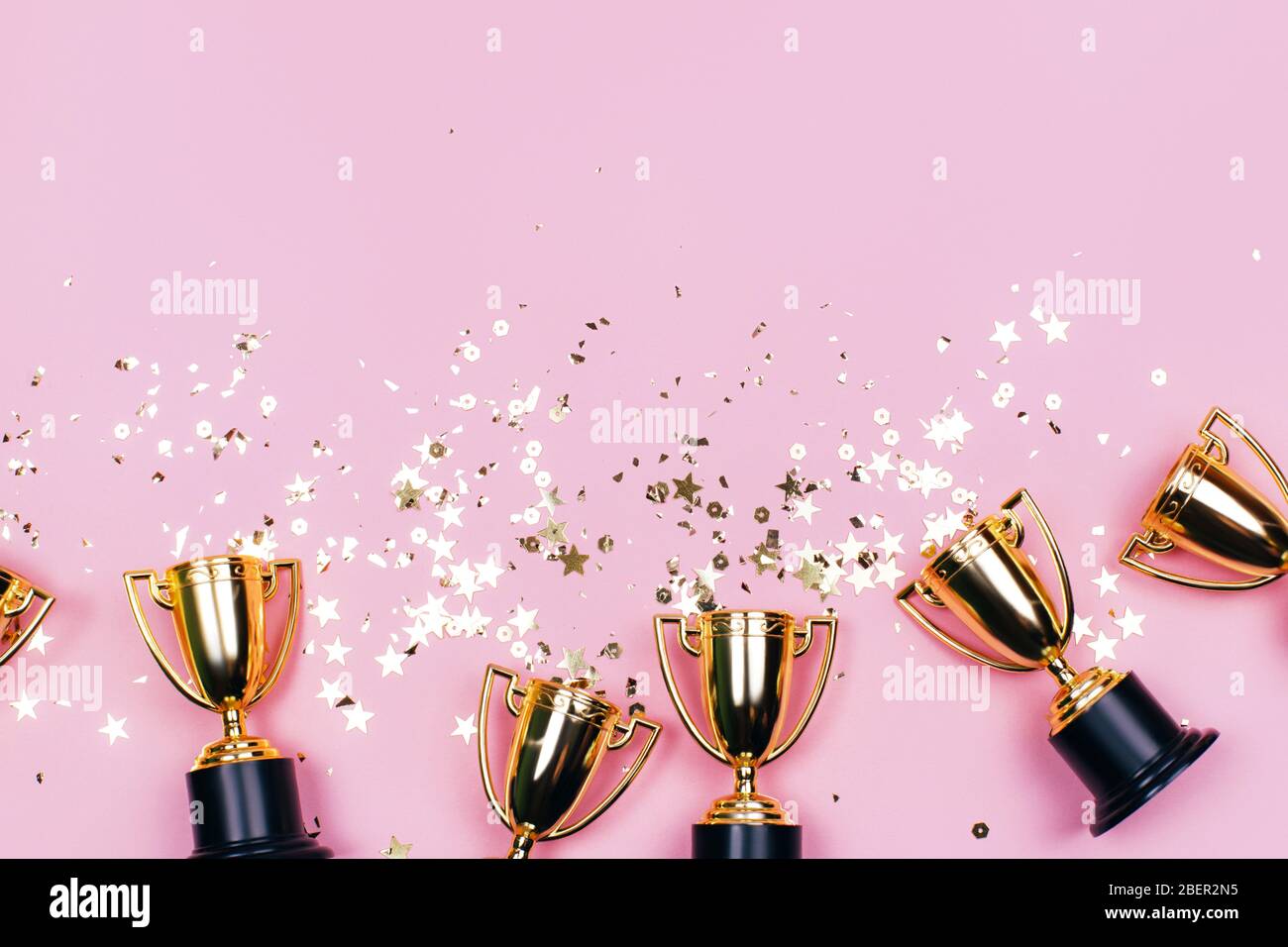 Golden winner cups with sparkles on a pink background with copy space ...