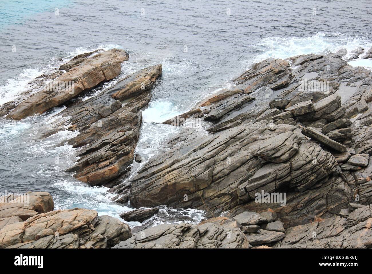 Rugged rocks layering out of the sea Stock Photo - Alamy