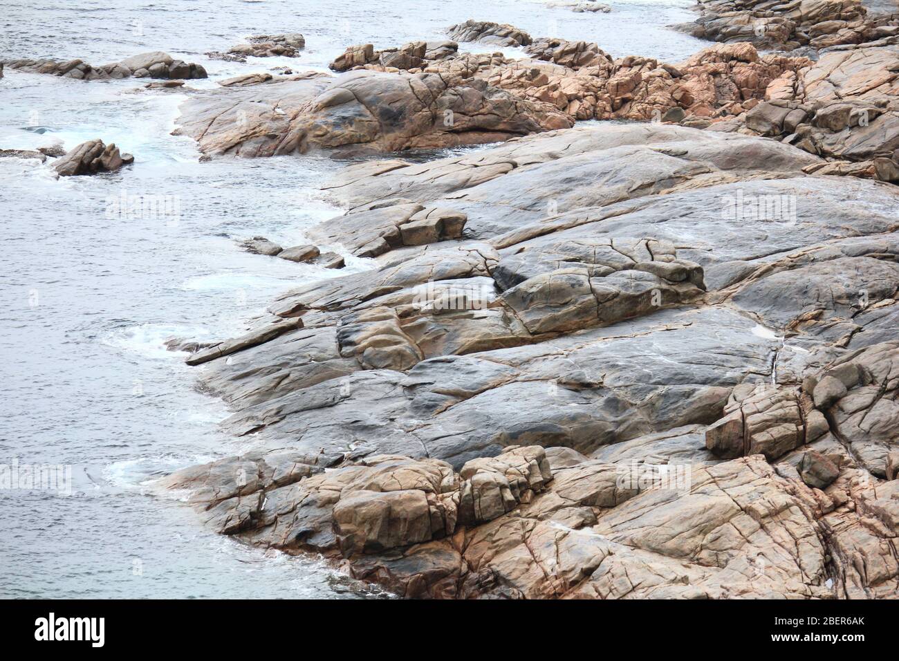 Rugged rocks layering out of the sea Stock Photo - Alamy