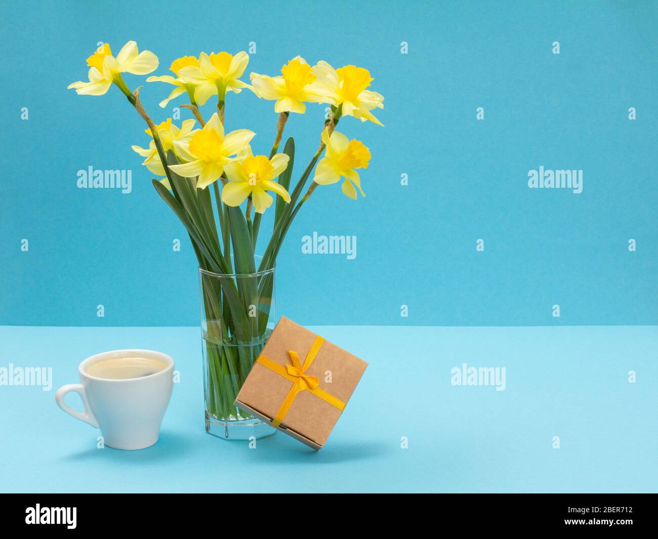 Bouquet of yellow daffodils in glass vase, a gift box and a cup of ...