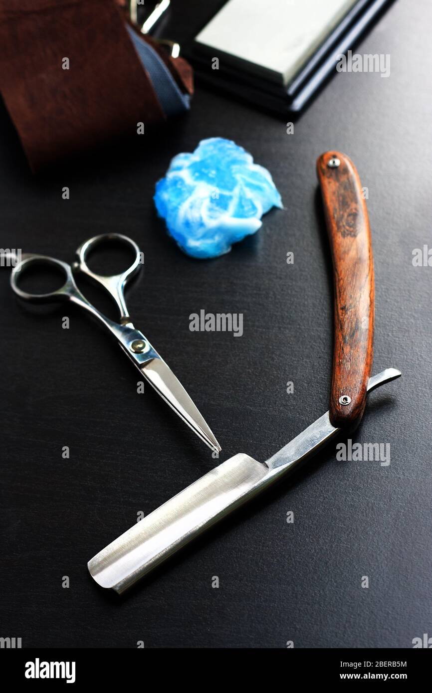 Straight razor, shaving foam, leather tool and scissors on black wooden ...