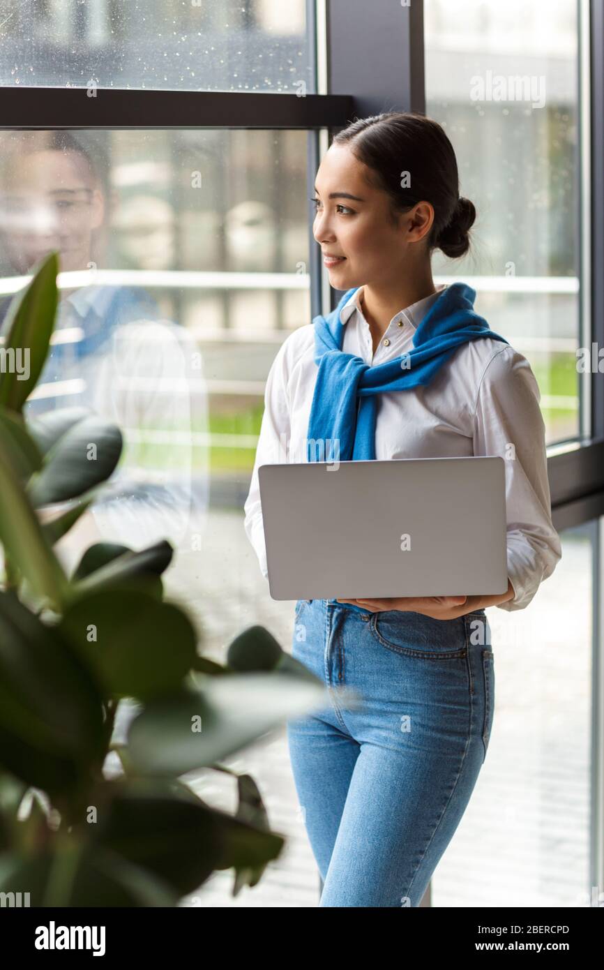 Image of young asian secretary woman standing by window and holding ...
