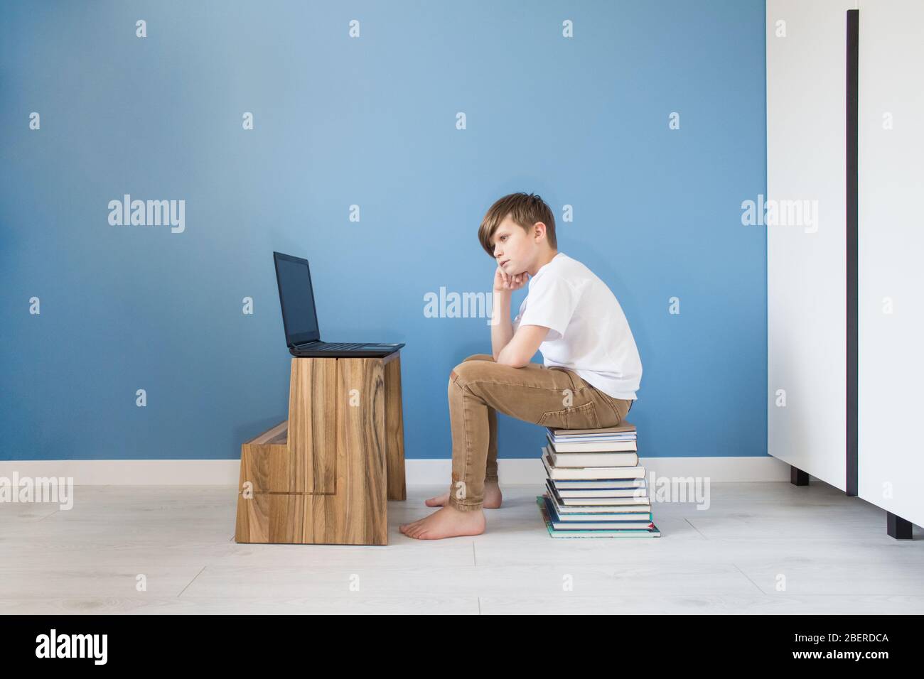 Sad child boy sitting on stack of books with his laptop, studying ...