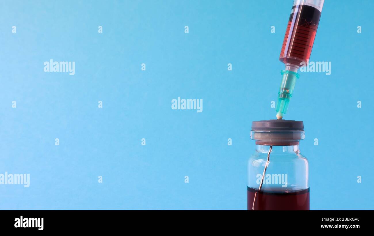 A syringe sticks out of a red liquid bottle. Isolated on a blue ...