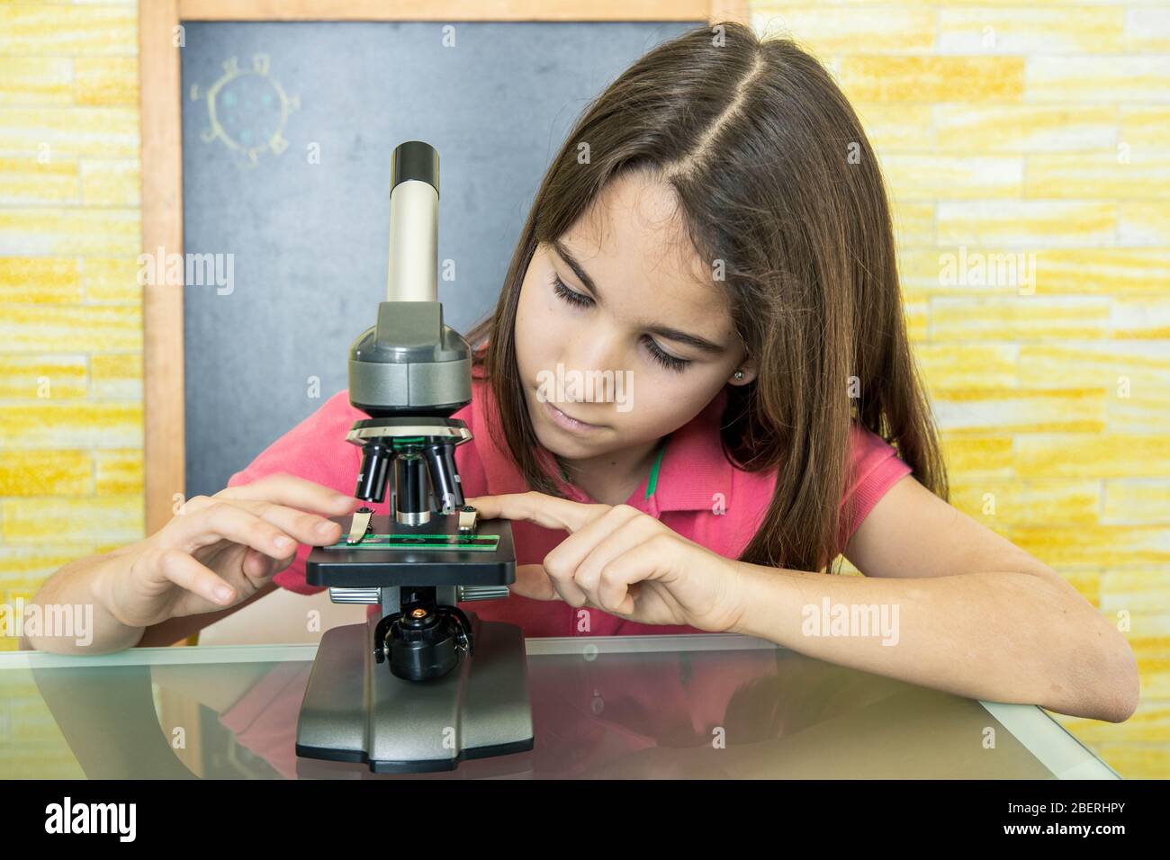 Little girl at home alone observing and studying under a microscope ...