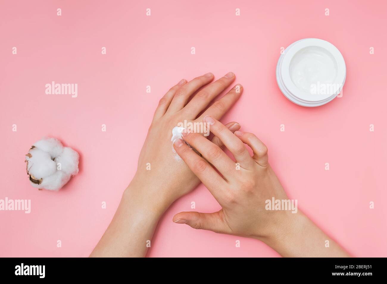 Woman moisturizing her hand with cosmetic cream with copy space on pink ...