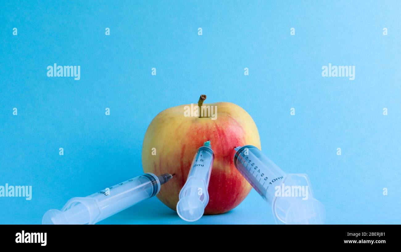 Three different medical syringes sticking deep into an apple on a blue ...
