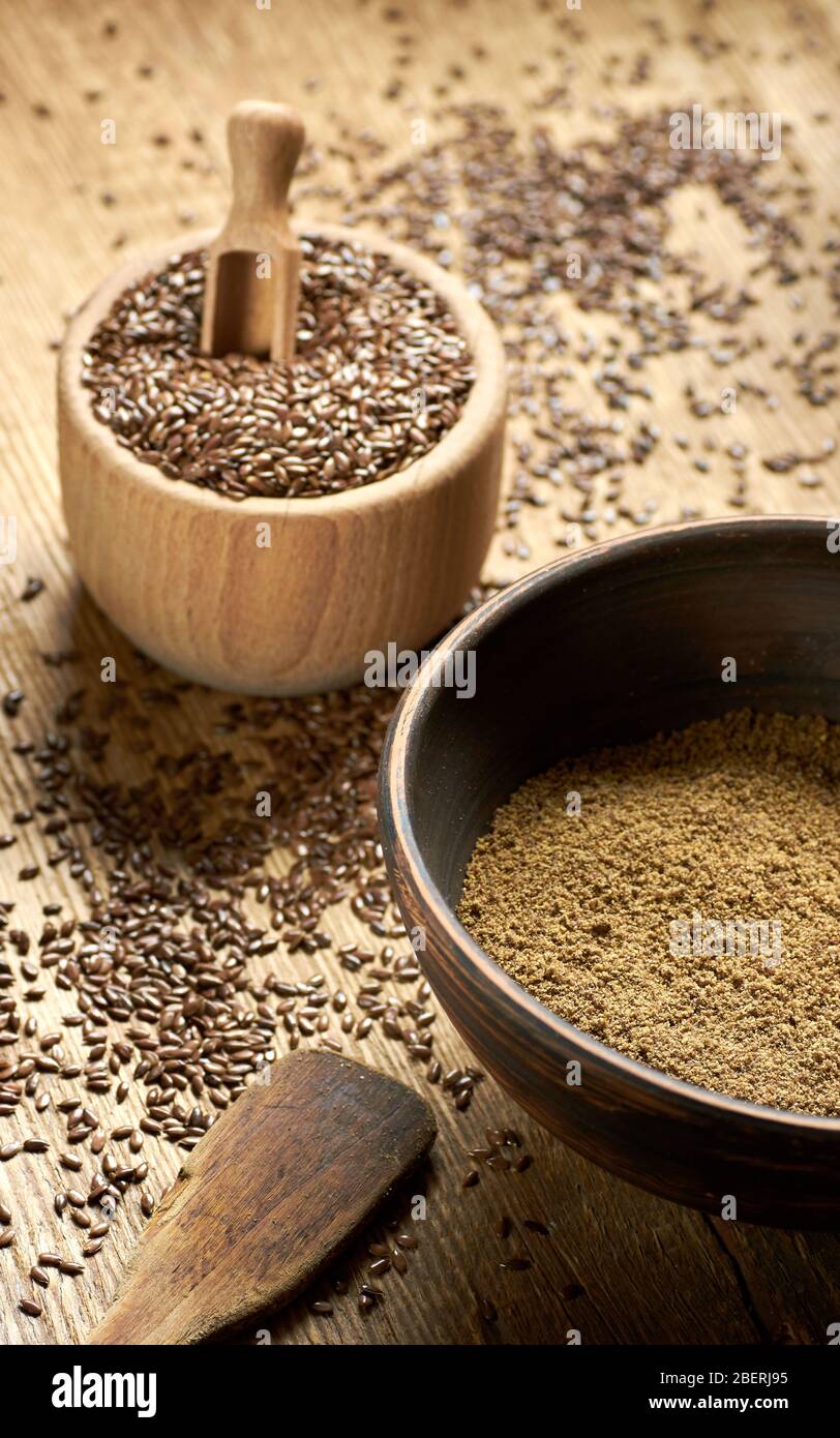 Flax seed coarse ground flour in a clay bowl with linseed wooden bowl nearby on rustic wood with ...