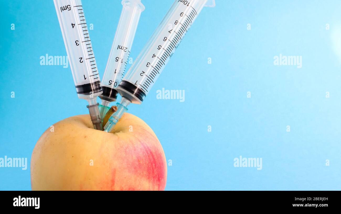 Three different medical syringes sticking deep into an apple on a blue ...