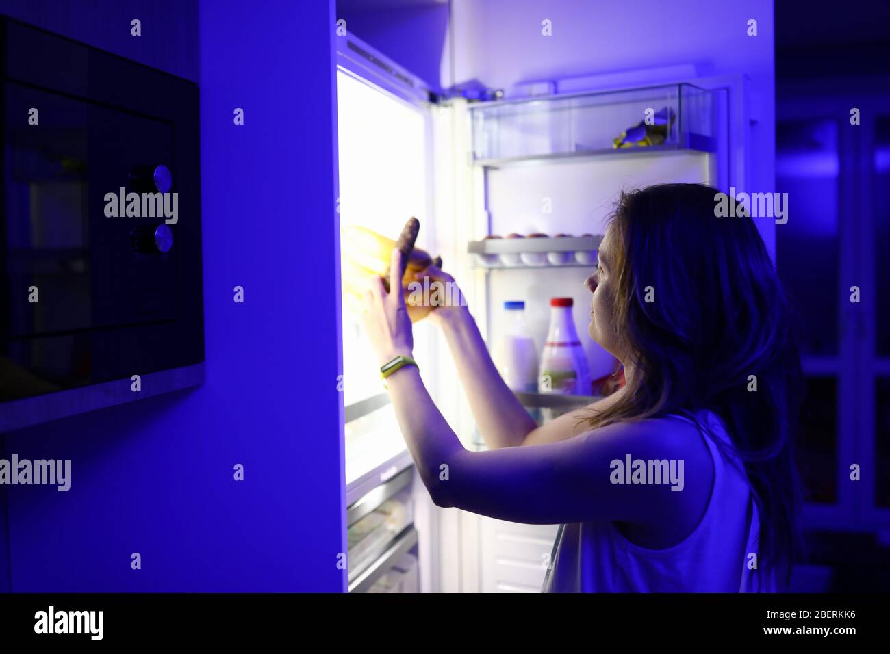Woman at night opened refrigerator and takes out food Stock Photo - Alamy