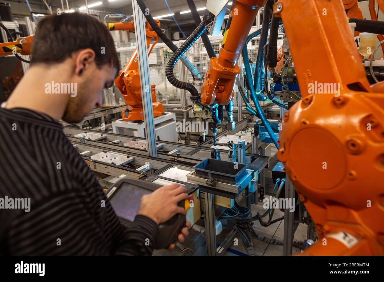 Repairman doing repair on automatic robot arms in huge automotive ...