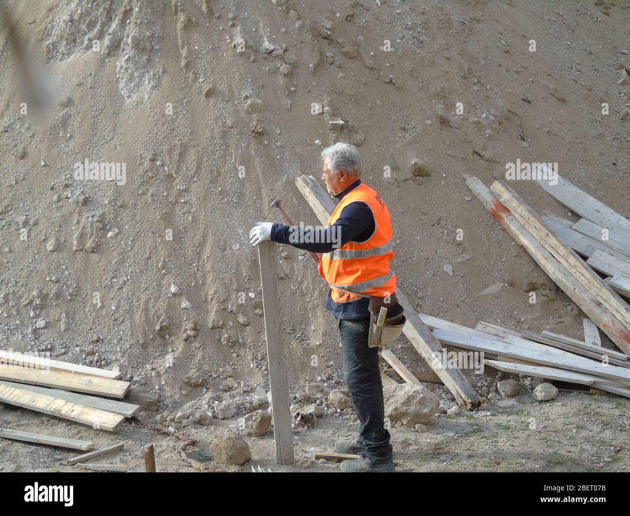 Worker on a construction site works with a a 2x4 Lamber and a Hammer ...