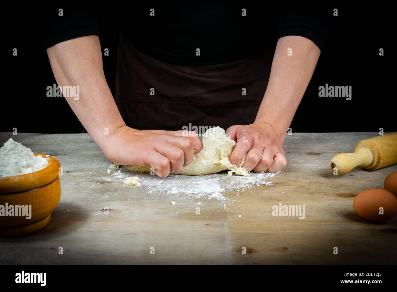 Man hands kneading bread dough on a wooden table with black background ...