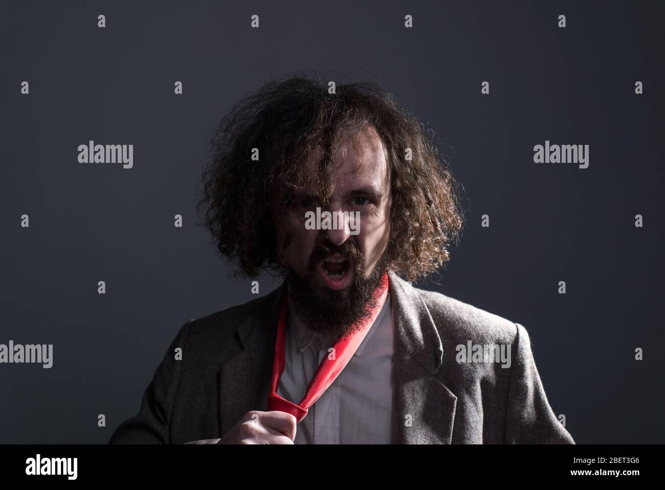 Studio portrait of a young bearded guy, with curly hair, pulls a red ...
