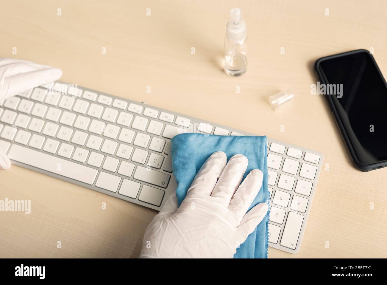 Hand with protective glove cleaning a keyboard with disinfectant. COVID ...