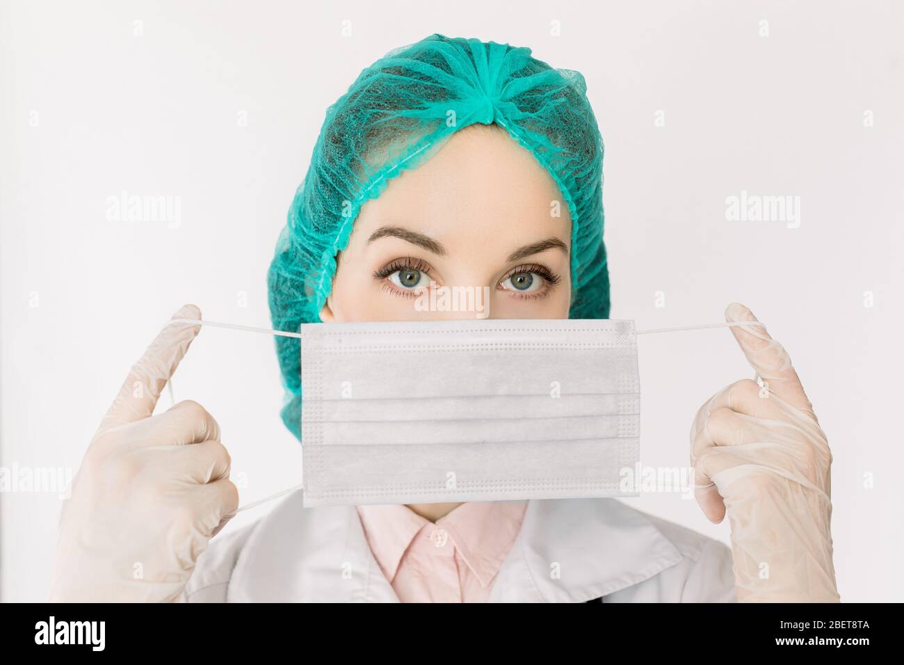 Close-up portrait of serious young nurse or doctor in cap, gloves and ...