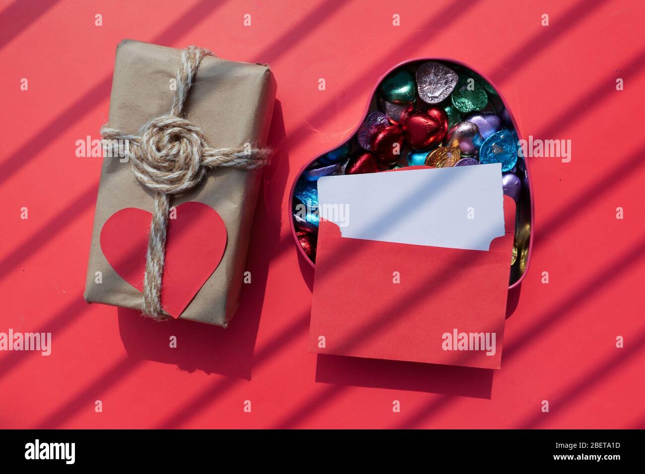 close up of candy in a heart shape box and envelope on red background ...