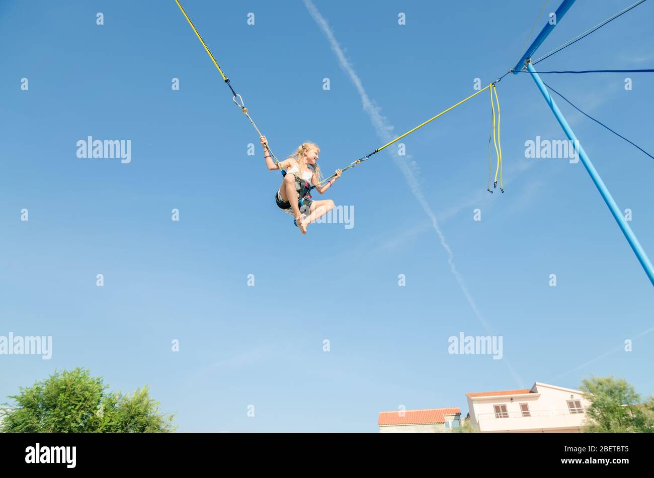 active little young teen girl jumping in trampoline high into the blue ...