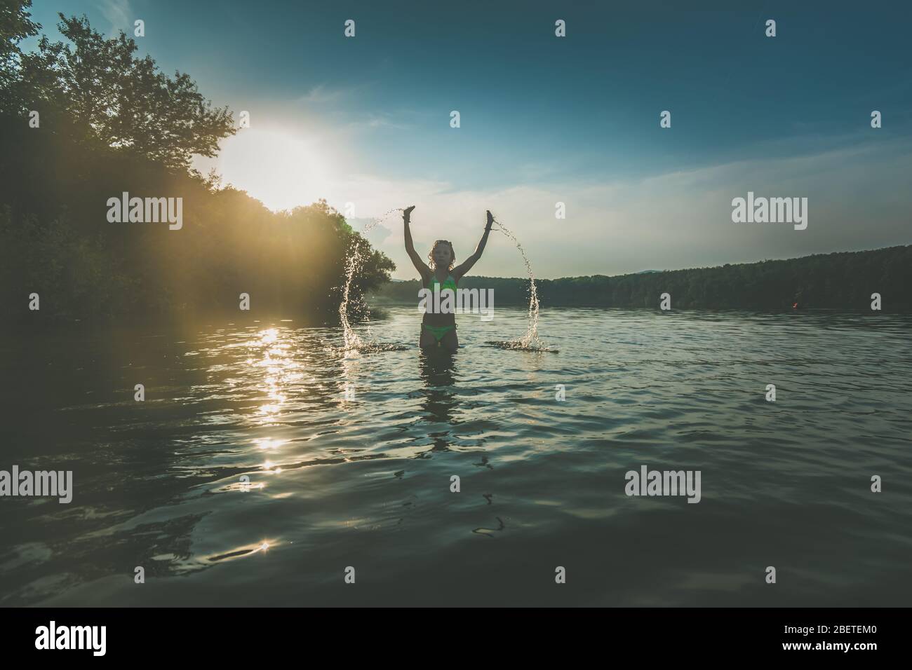 cute girl with long blond hair having fun in pond in magic golden hour ...