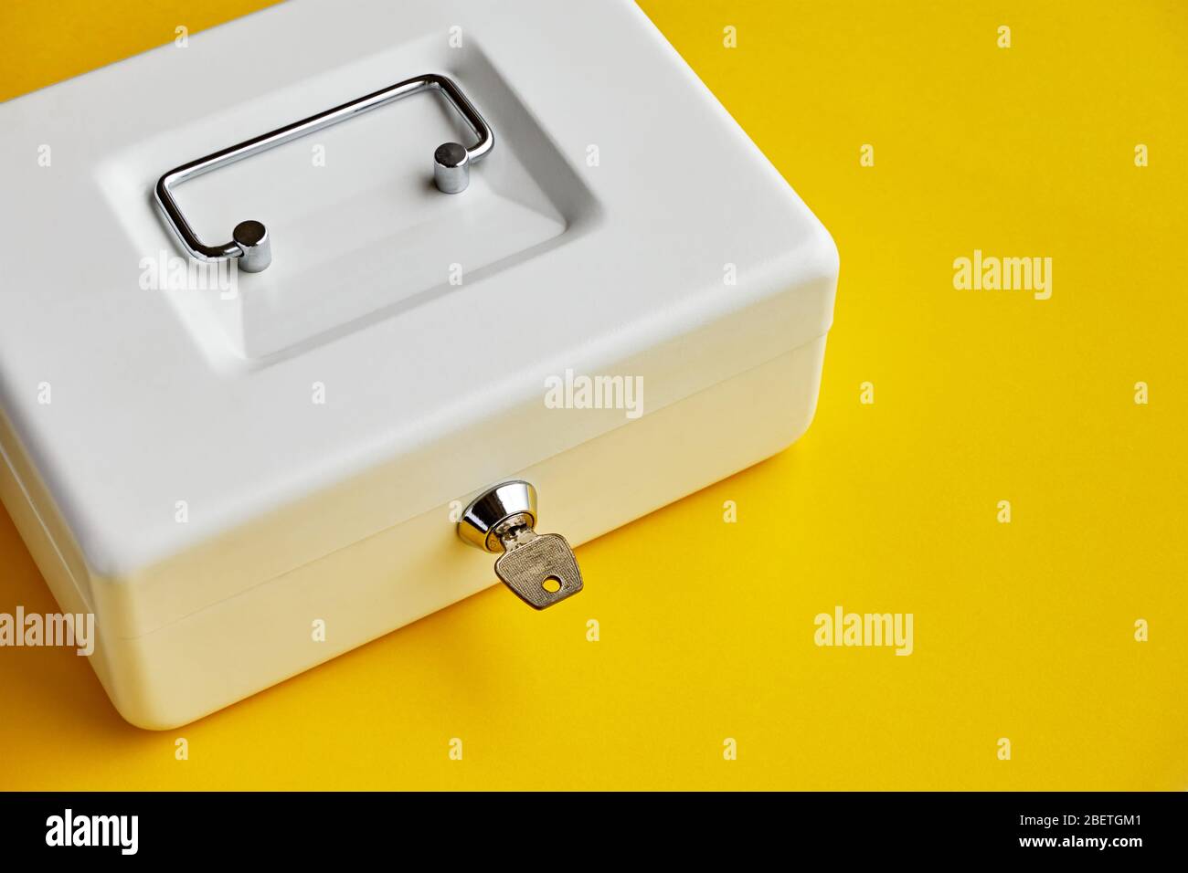 Close up of small white closed cashbox or money box with key in lock on ...