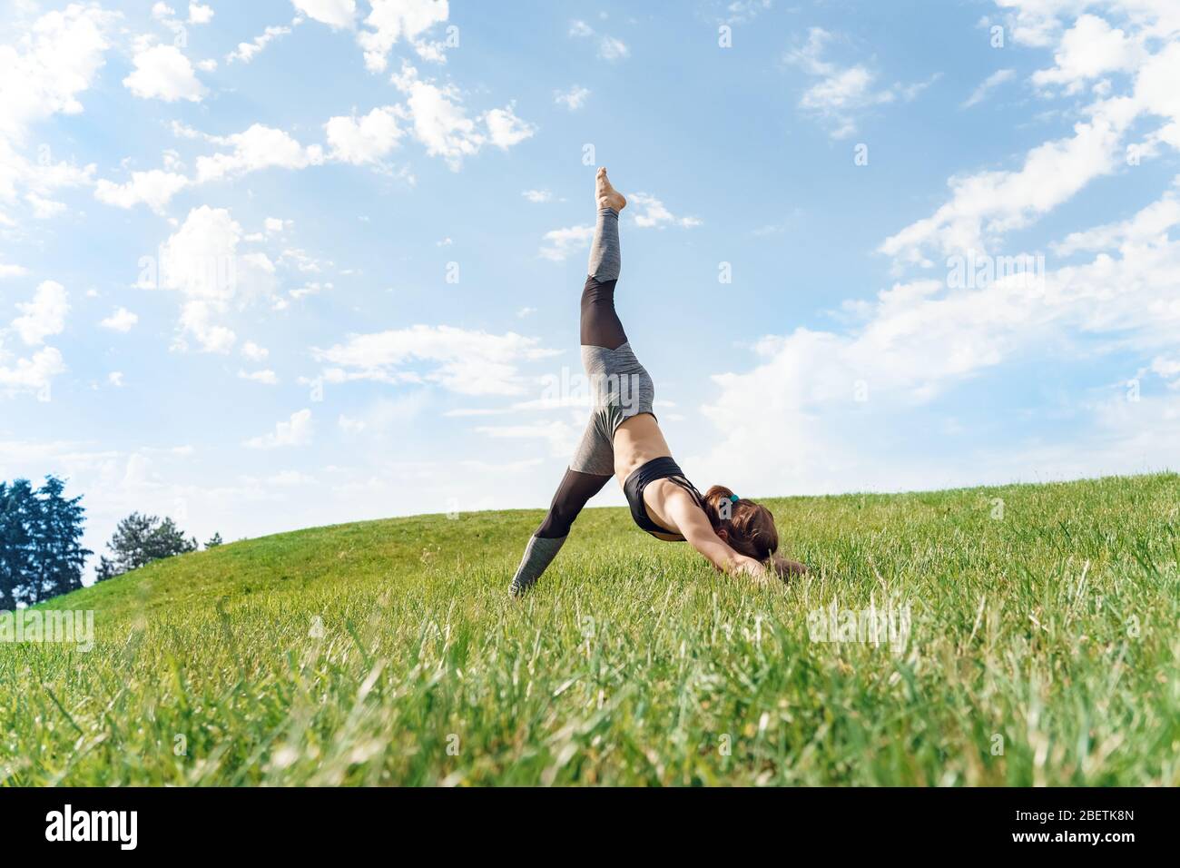 Healthy Lifestyle. Young woman outdoors doing yoga standing on arms leg ...