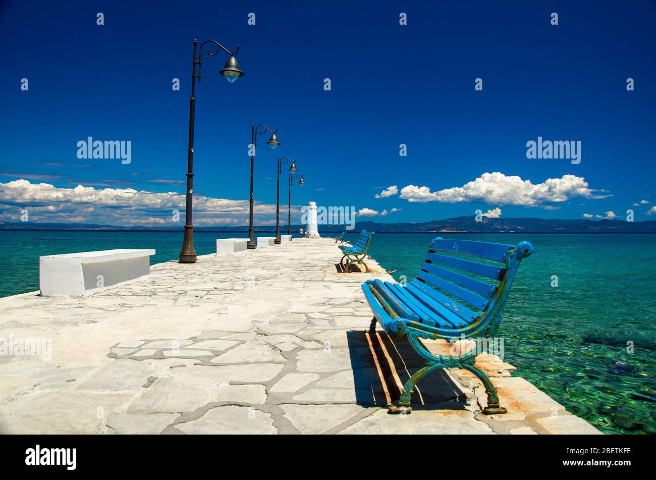 White pier jetty with bench, lampposts and lighthouse on blue paradise ...