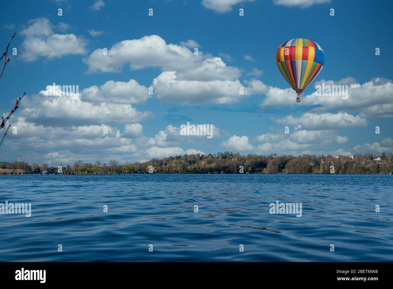 a colourful hot air balloon flies over the blue water of a lake Stock ...