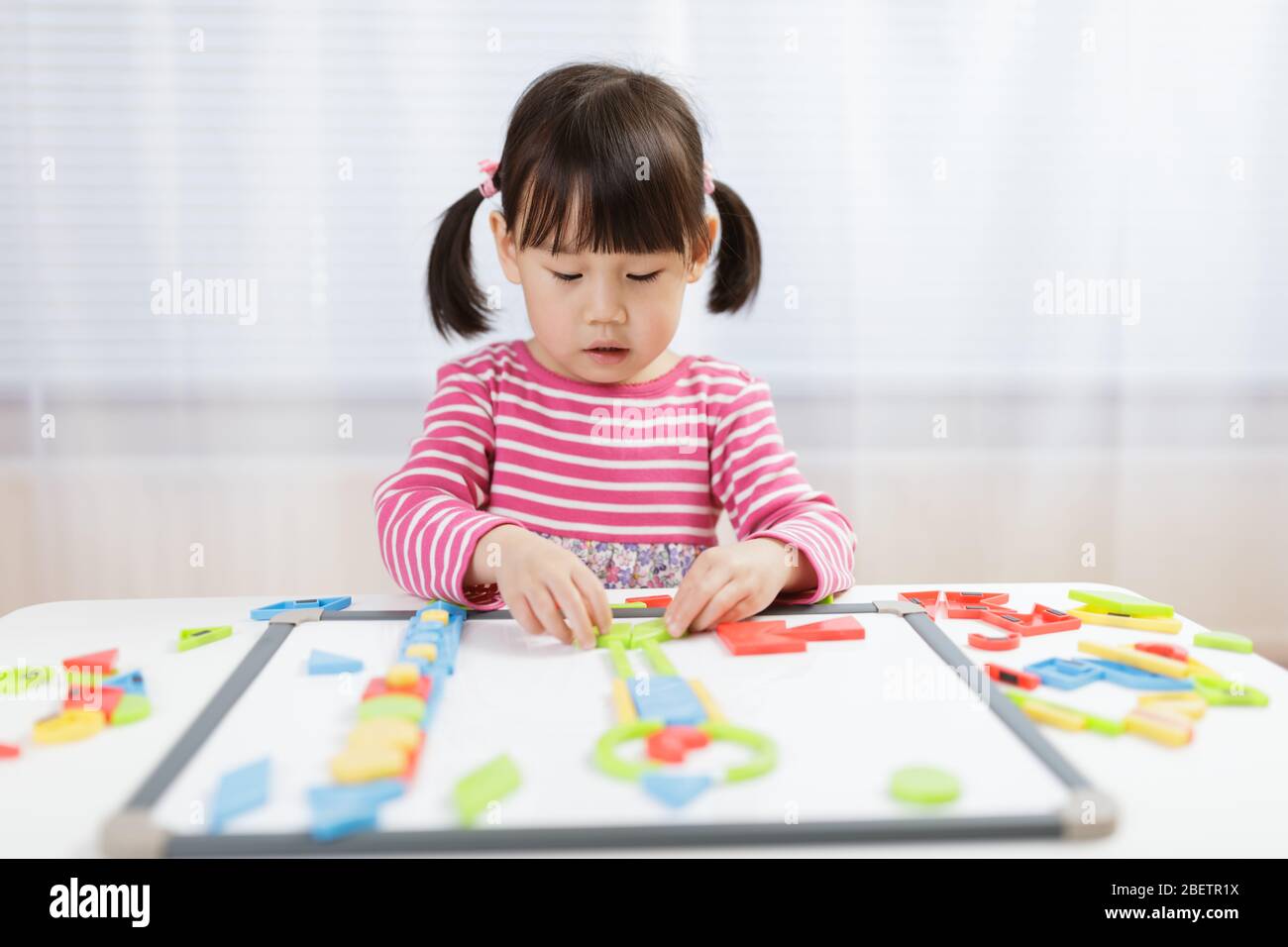 toddler girl playing creative shape blocks at home against white ...