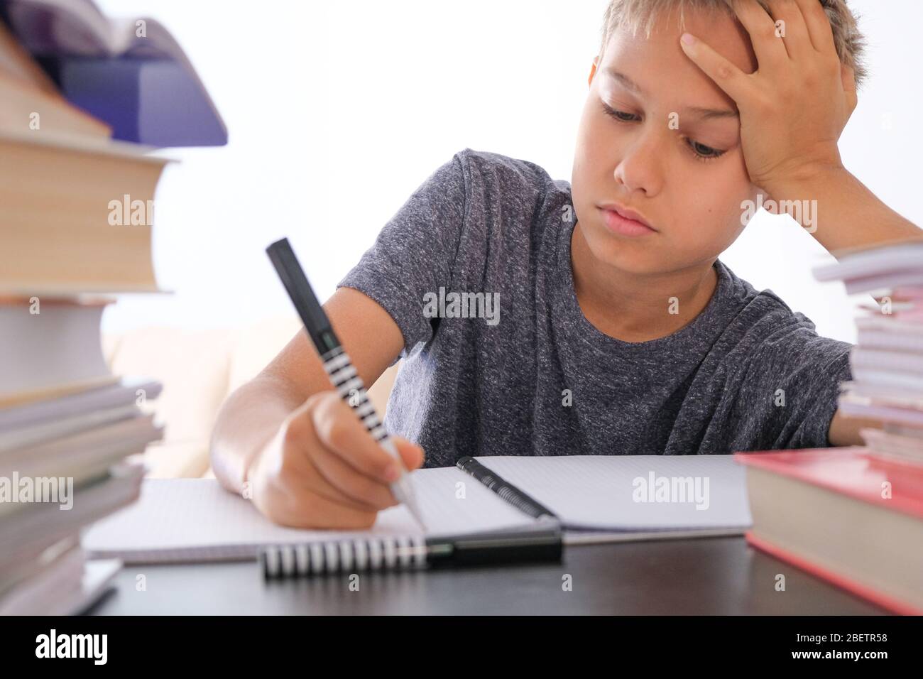 Schoolboy sitting among pile of books, textbooks, school exercise books ...
