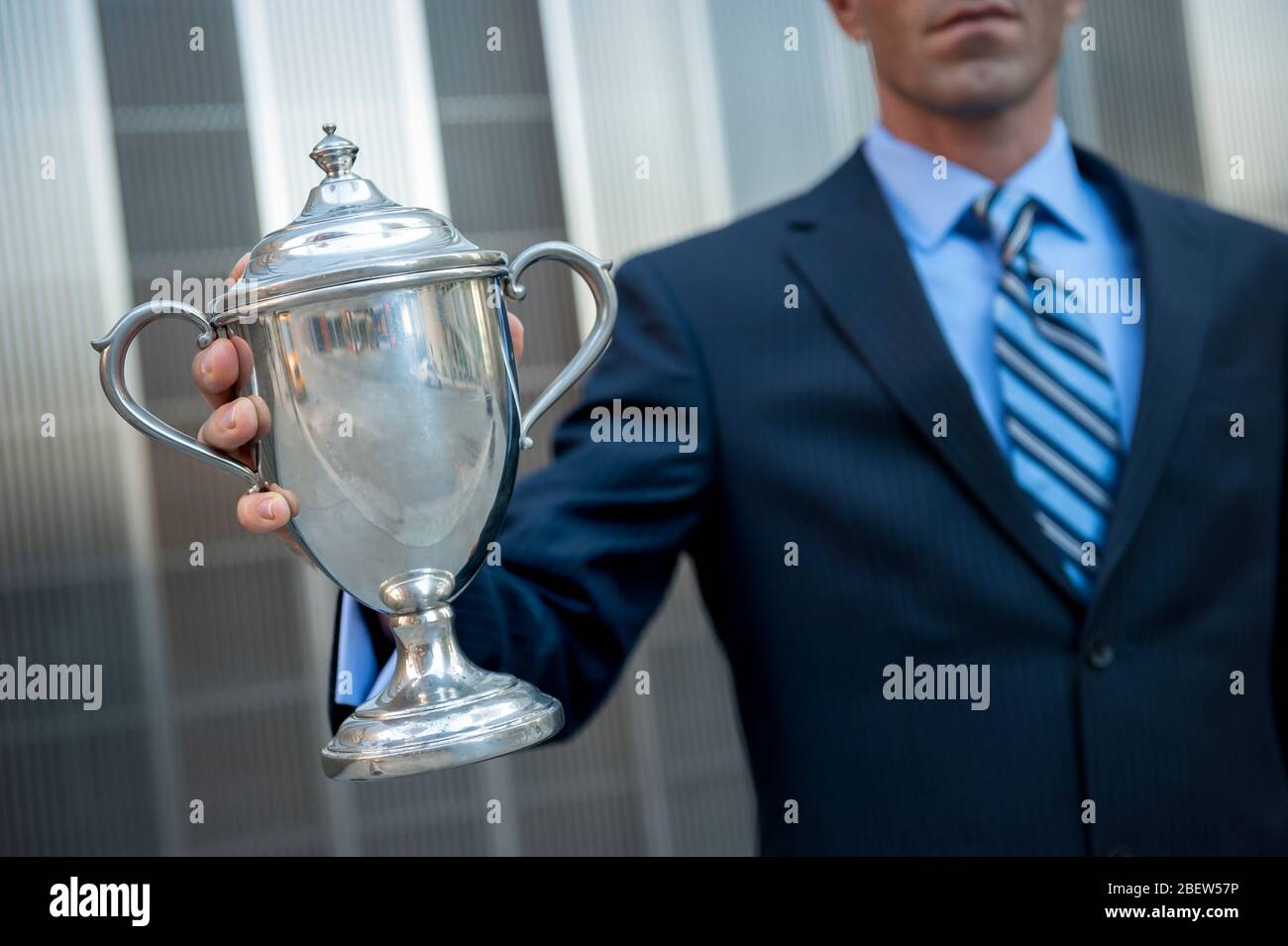 Proud businessman holding up a silver trophy outdoors in front of shiny ...
