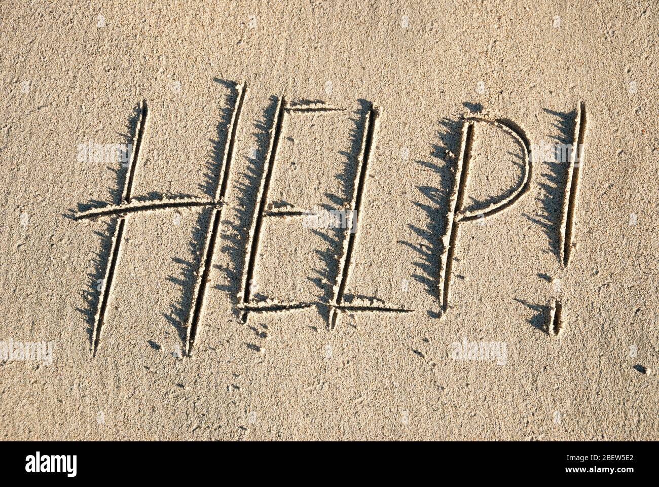 Urgent Help! message handwritten on the beach with textured capital ...