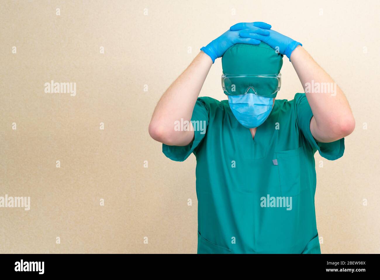 Doctor in green suit and blue gloves hiding face under mask an hat ...
