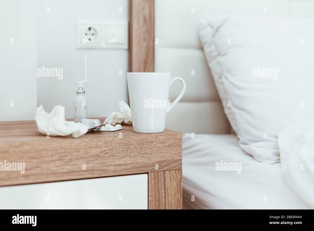 Medicines, pills, nose drops, tissues and hot drink cup on bedside ...