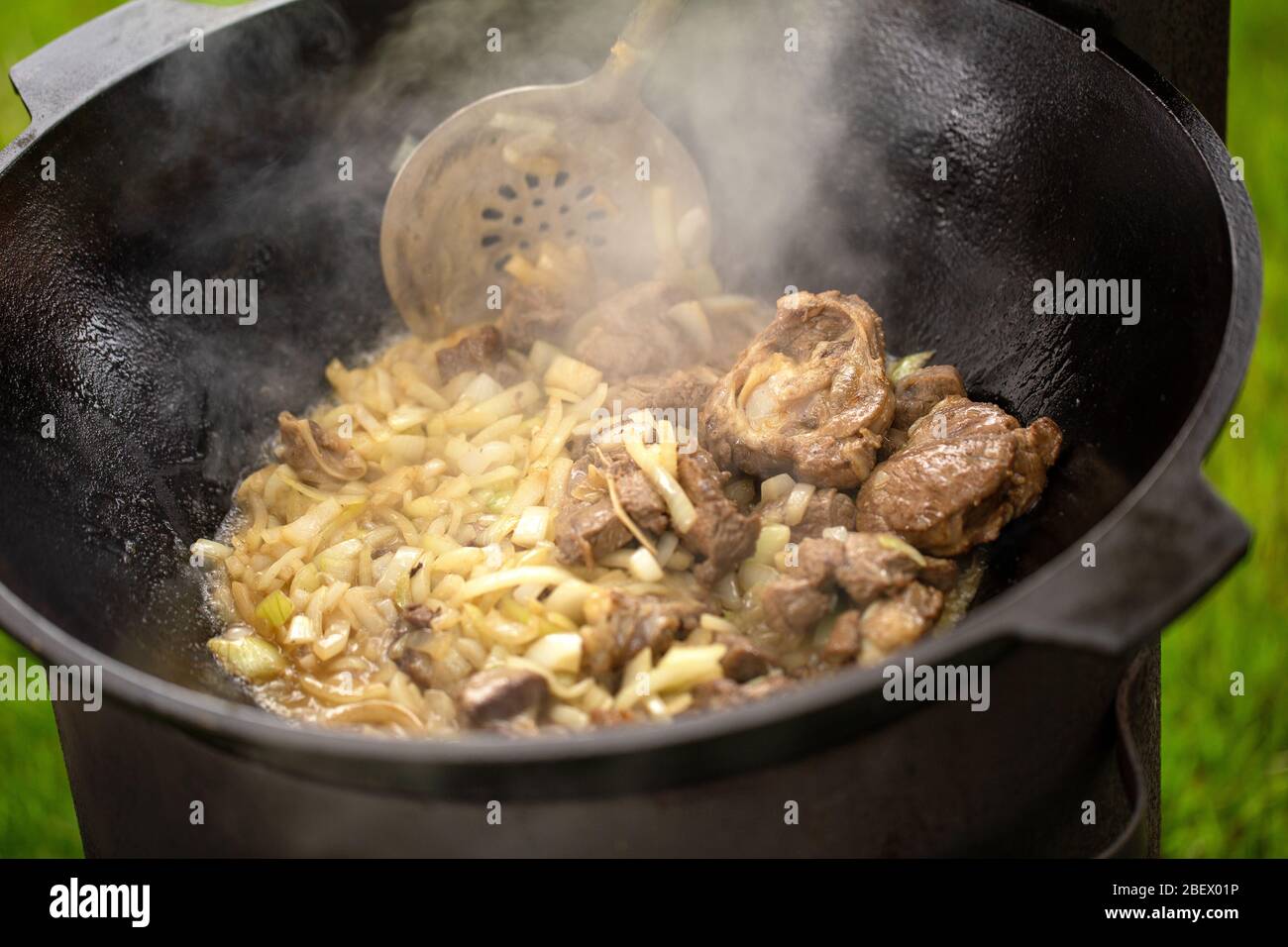 Cooking tasty pilaf in cast iron cauldron. Mutton meat fried with onion ...