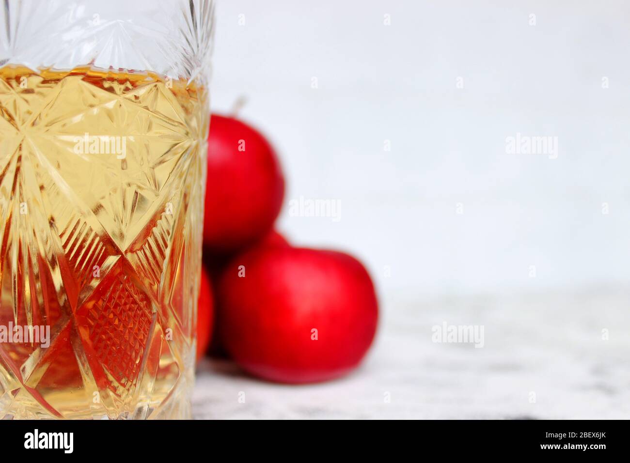 Light apple juice in a crystal glass and ripe red apples on a white ...