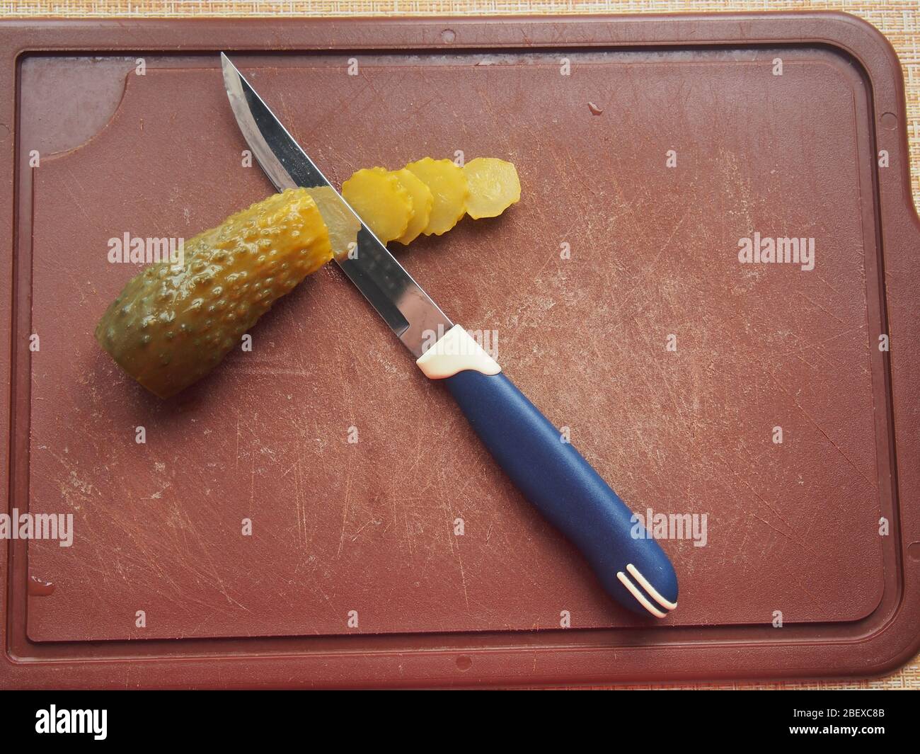 On the cutting Board are a pickle and a knife. The pickle is cut into ...