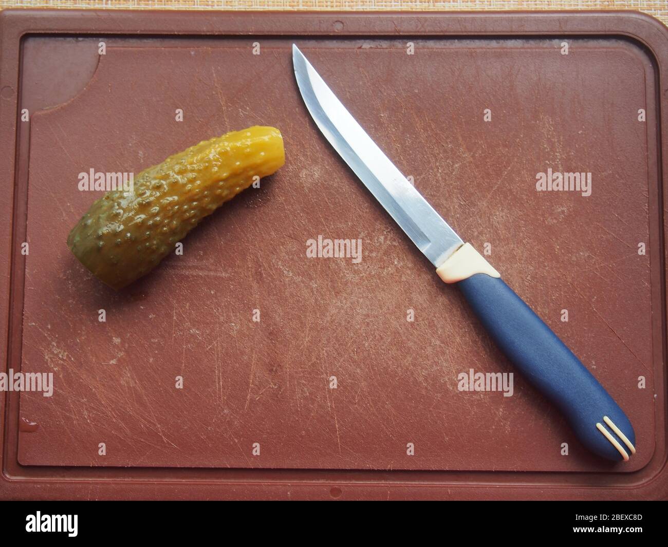 On the cutting Board are a pickle and a knife. The pickle is cut into ...