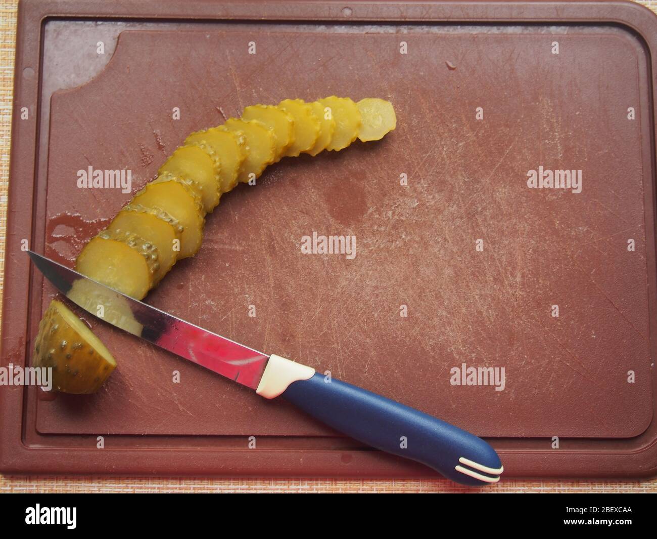 On the cutting Board are a pickle and a knife. The pickle is cut into ...