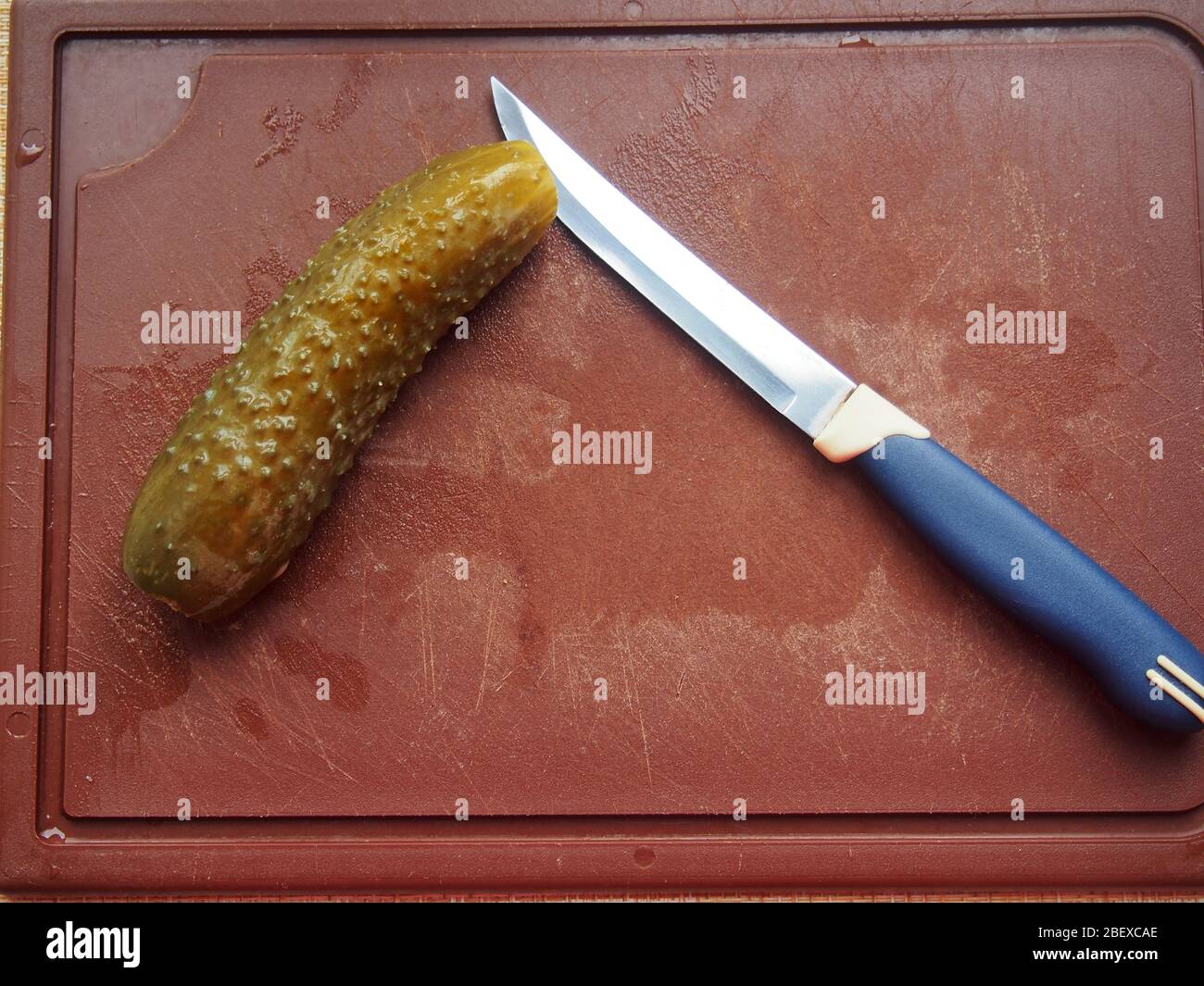 On the cutting Board are a pickle and a knife. The pickle is cut into ...