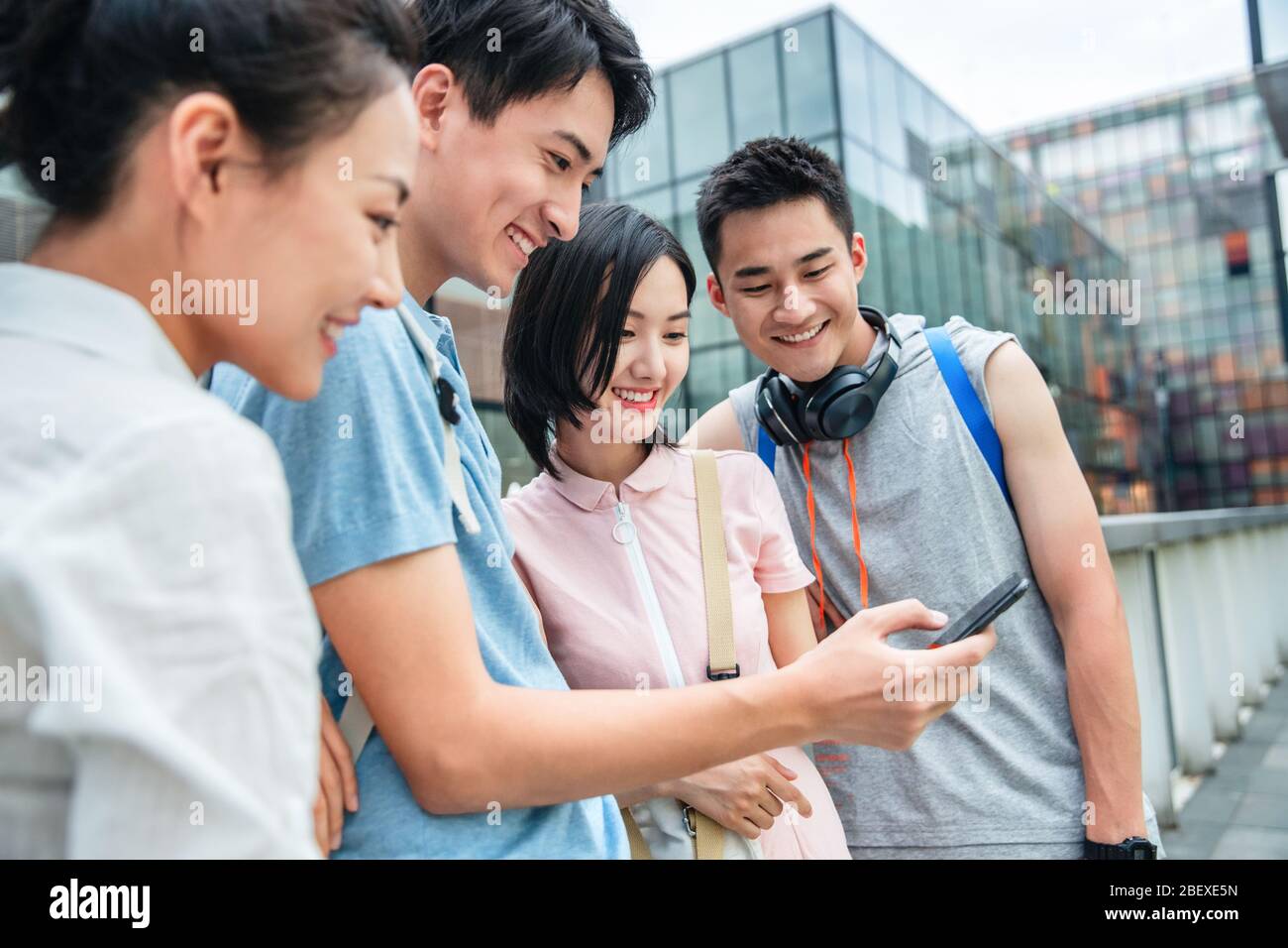 Outdoor four college students watch mobile phone Stock Photo - Alamy
