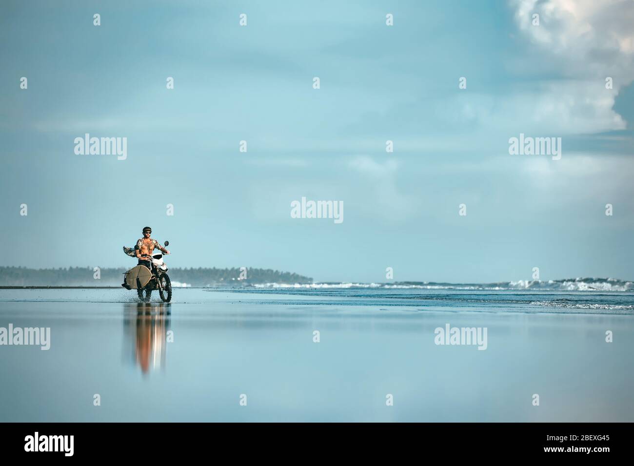 Authentic male surfer rides with surfboard on motorcycle at ocean beach ...