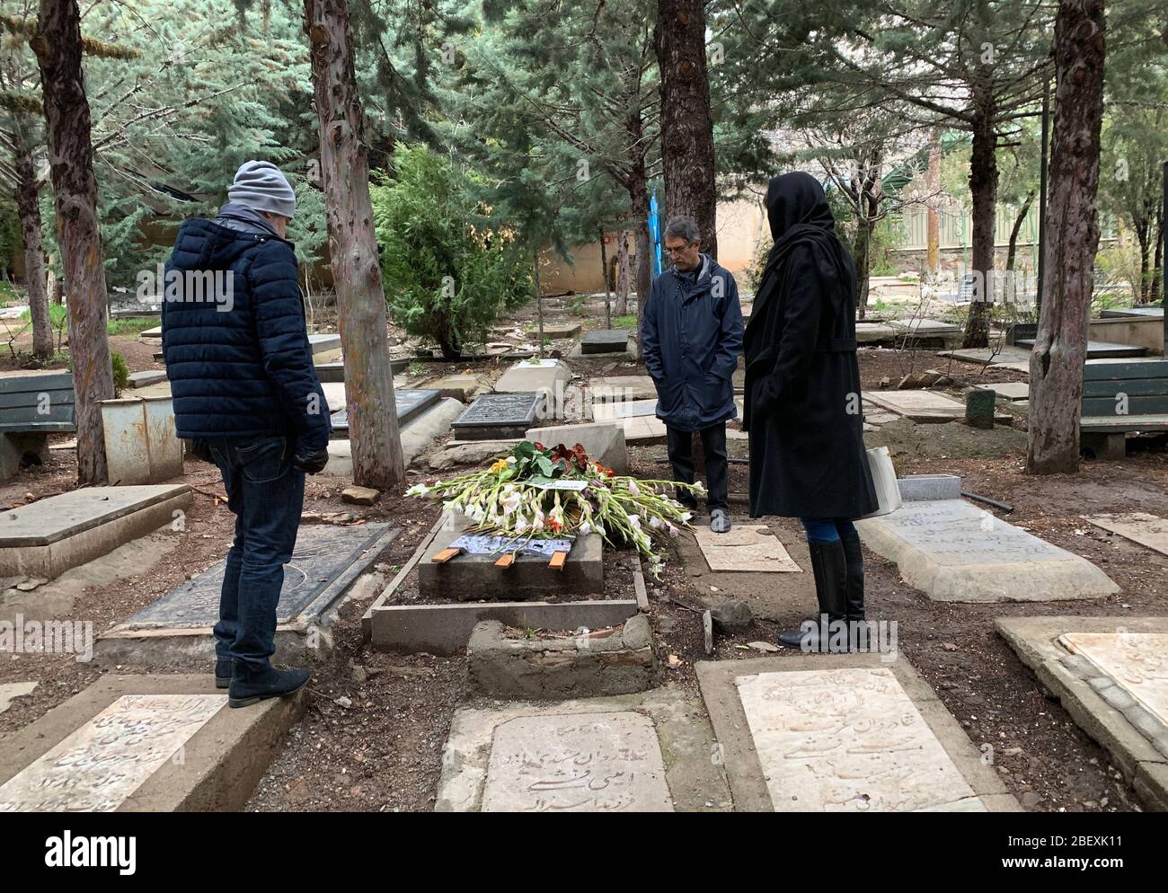 08 April 2020, Iran, Teheran: Three Iranians stand at a grave in the ...